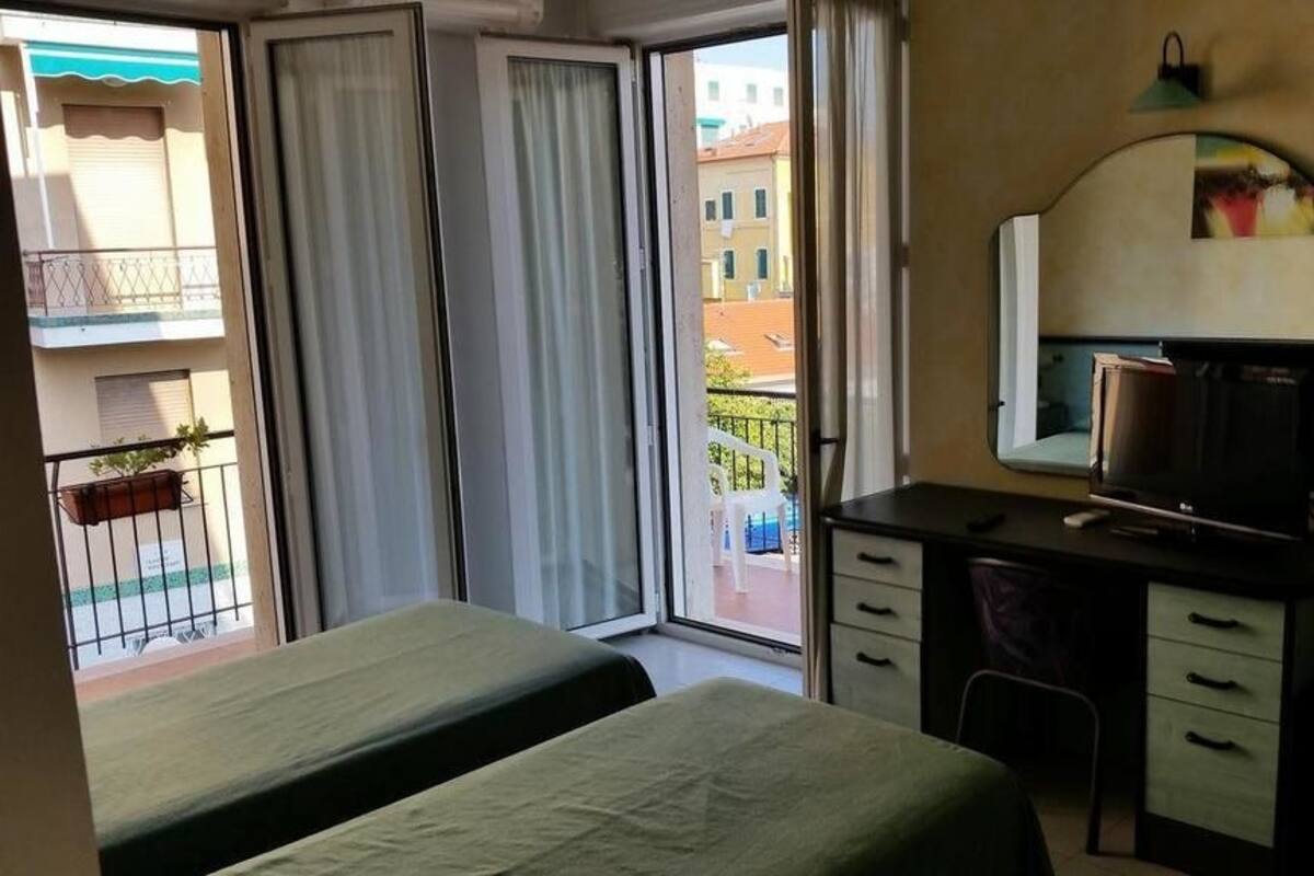 Quarto de hotel com cama, escrivaninha, cadeira, espelho e janela com cortinas.