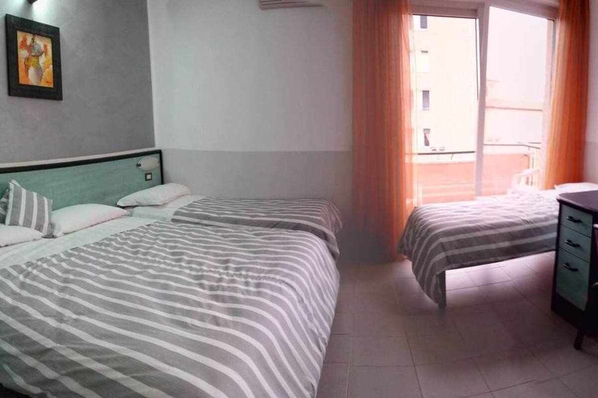 Quarto de hotel com duas camas, uma escrivaninha, uma televisão e uma janela com cortinas.