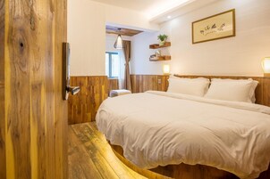 Quarto de madeira com cama, mesa de cabeceira, prateleira na parede com uma planta e um letreiro emoldurado.