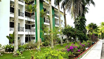 Um hotel com vários andares e varandas, cercado por vegetação exuberante e plantas em vasos.