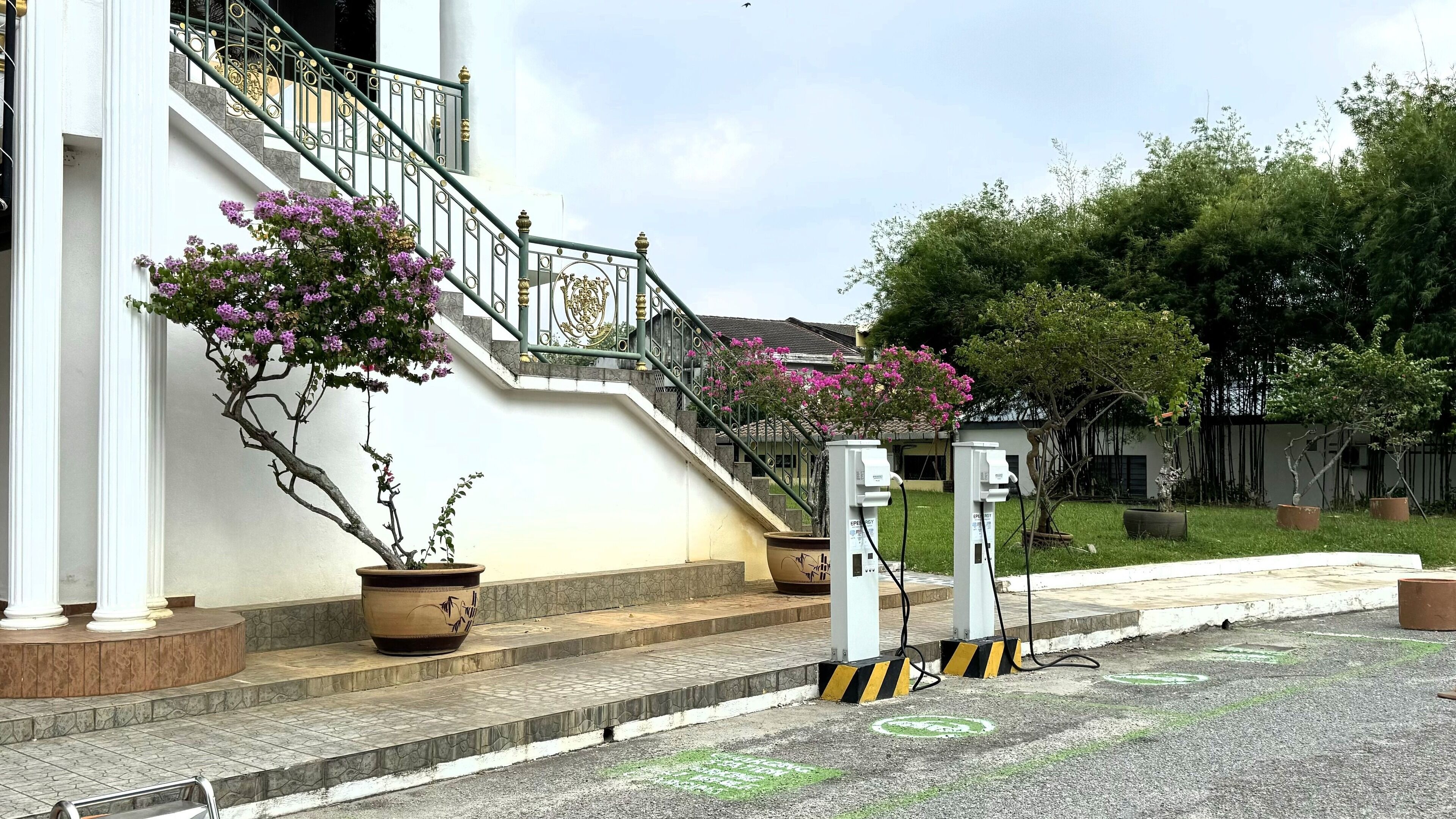 Edifício com escadaria, plantas em vasos e área de estacionamento com pontos de carregamento para veículos elétricos.