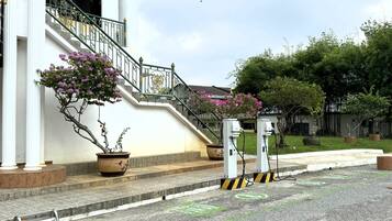 Edifício com escadaria, plantas em vasos e área de estacionamento com pontos de carregamento para veículos elétricos.