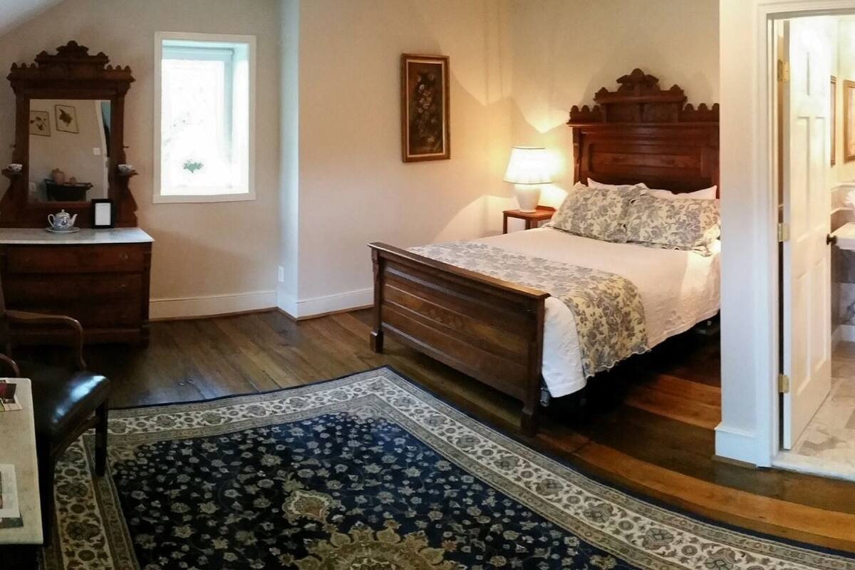 Um quarto com cama de madeira, mesa de cabeceira com luminária, cômoda, espelho e um tapete grande.