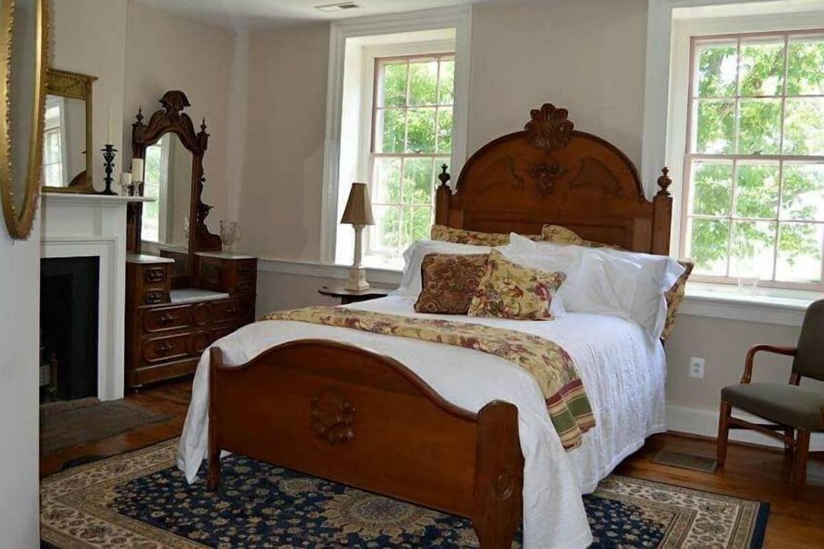 Quarto com uma cama grande, penteadeira, espelho e duas janelas.