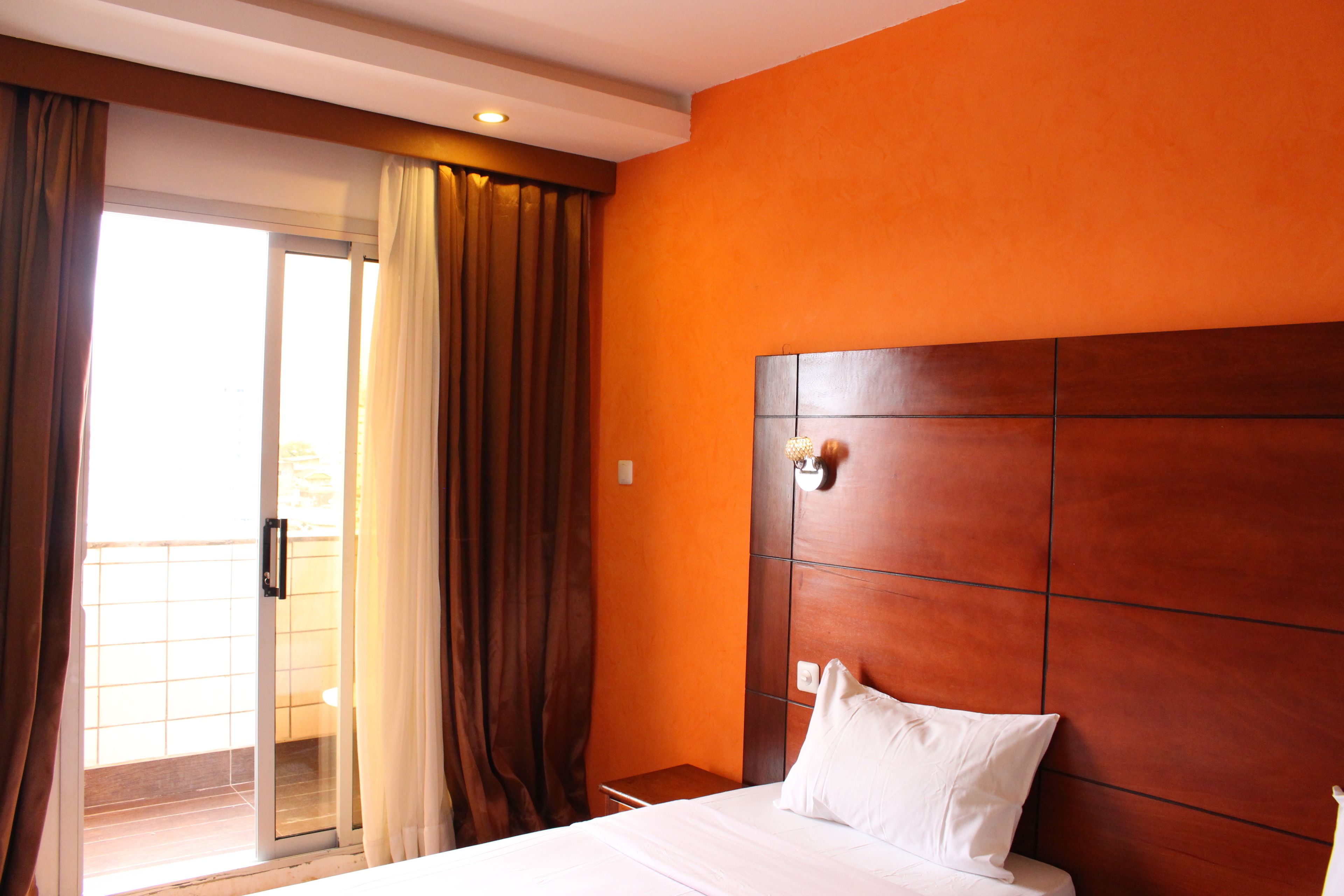 Quarto de hotel com uma cama grande, cabeceira de madeira e porta de vidro deslizante para uma varanda.