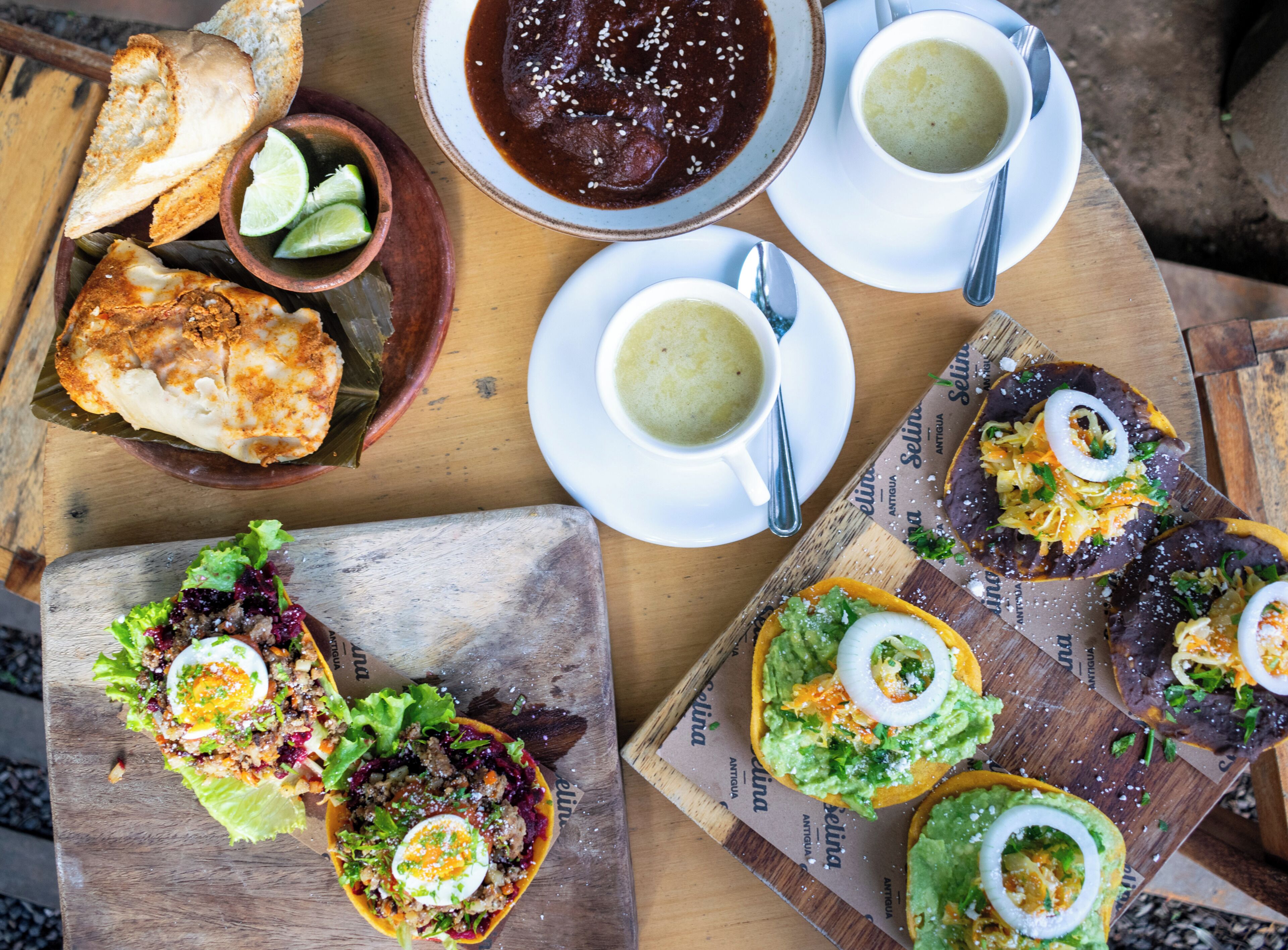 Diversos pratos, incluindo tacos, uma tigela de sopa e pão sobre uma mesa de madeira.