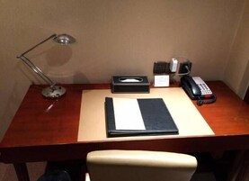 Balcão de hotel com abajur, telefone, uma caixa e uma pasta dobrada.
