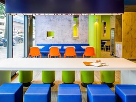 Uma área de estar moderna com uma mesa comprida, várias cadeiras e banquetas coloridas.