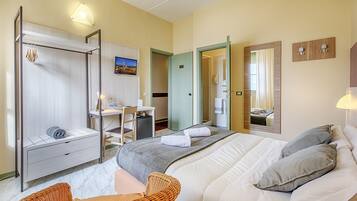 Quarto de hotel com cama, escrivaninha, cadeira, guarda-roupa e banheiro visível por uma porta aberta.