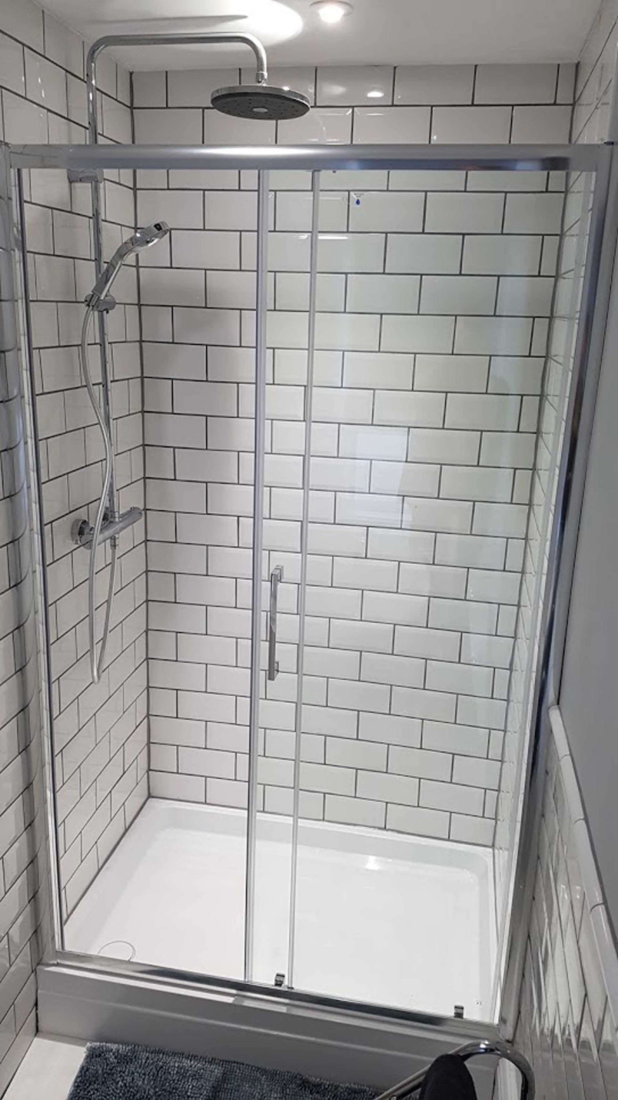 Um chuveiro com paredes de azulejos brancos e piso transparente, protegido por um box de vidro.