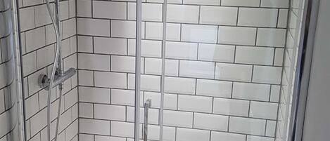 Um chuveiro com paredes de azulejos brancos e piso transparente, protegido por um box de vidro.