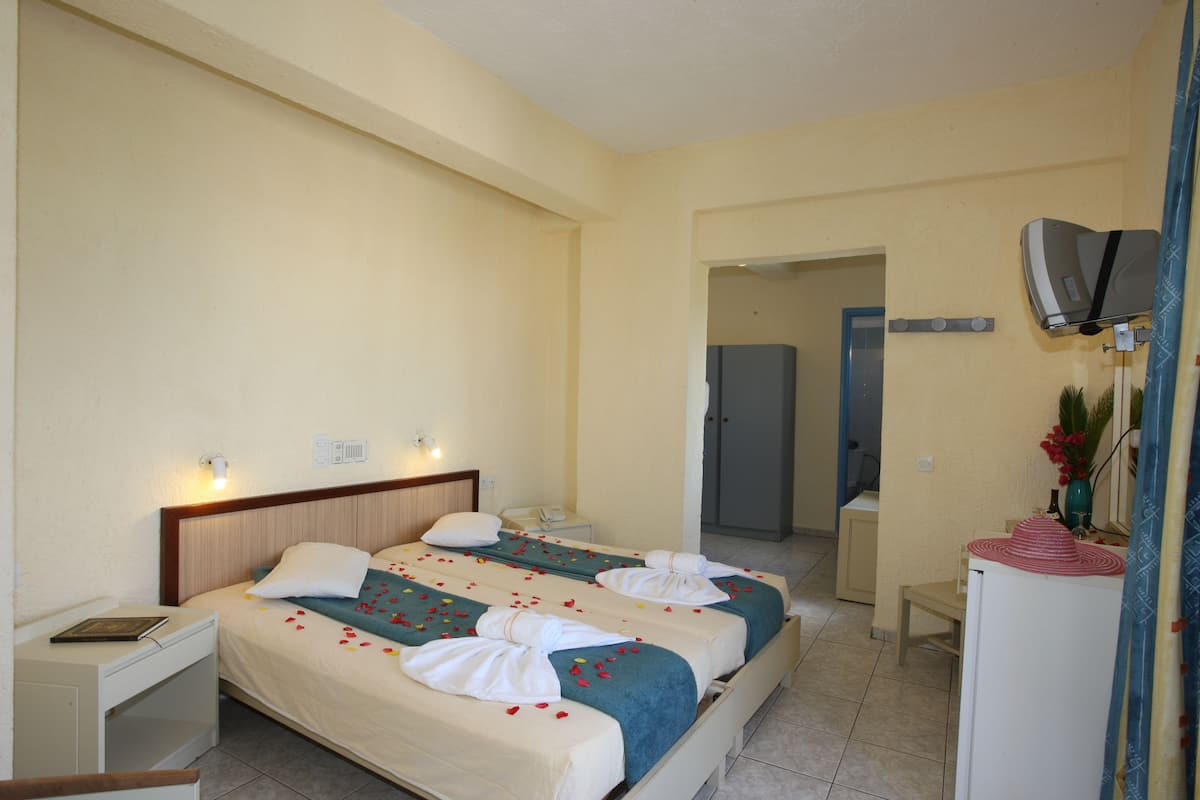 Quarto de hotel com duas camas, uma escrivaninha, uma cadeira, uma mesinha e uma televisão.