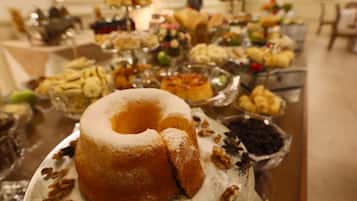 Uma mesa de buffet com diversos pratos, incluindo um bolo bundt central e sobremesas variadas.