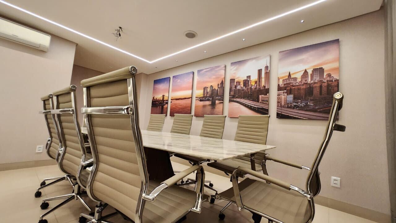 Uma sala de conferências com uma mesa comprida, quatro cadeiras e pinturas da paisagem urbana nas paredes.