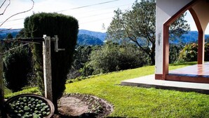 Jardim bem cuidado com um portão de madeira, um canteiro circular com plantas e vista para uma paisagem montanhosa.