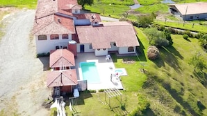 Uma casa grande com vários telhados vermelhos, piscina e gramado bem cuidado.