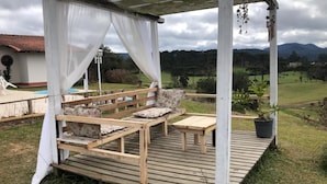 Área de estar coberta ao ar livre, com móveis de madeira e uma planta em vaso.