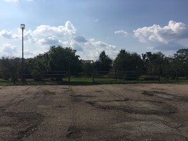 Campo aberto com cerca de metal e árvores ao fundo.