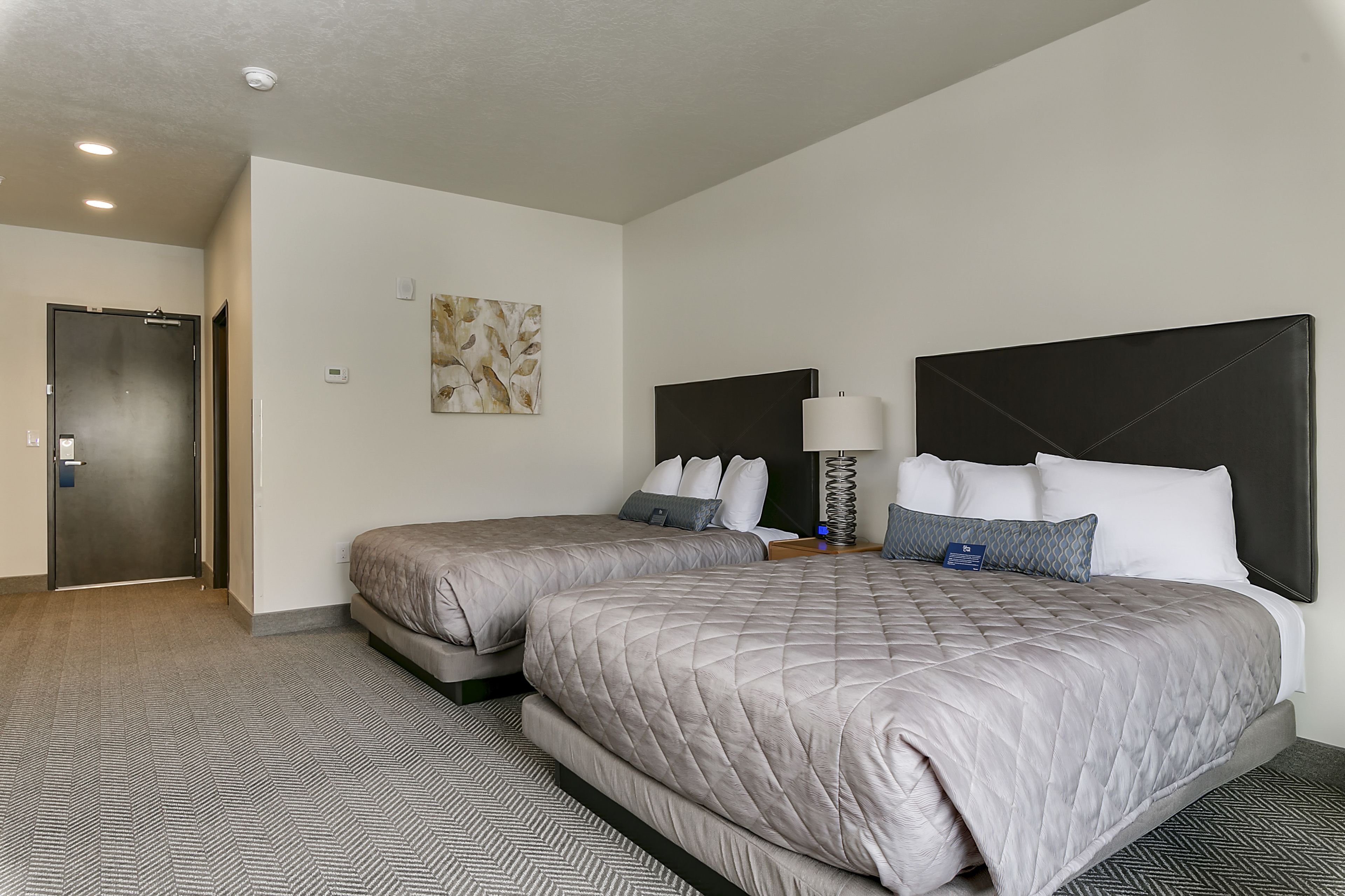 Quarto de hotel com duas camas, uma porta, uma obra de arte fixada na parede e uma luminária.