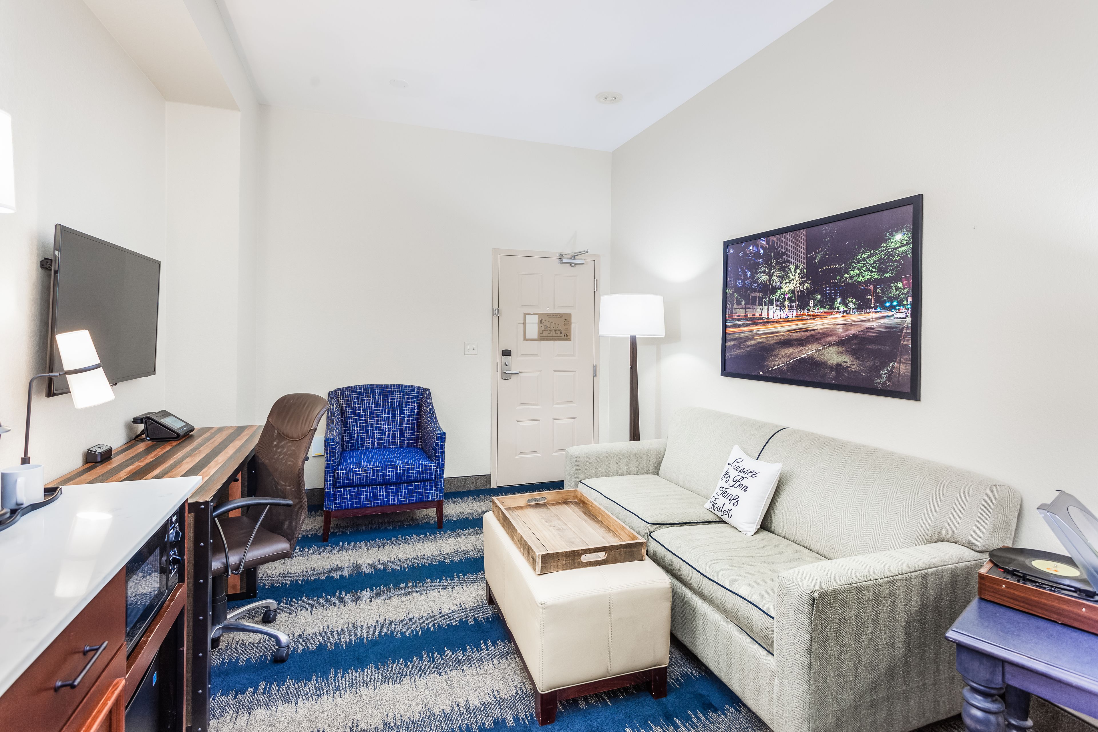 Quarto de hotel com escrivaninha, cadeira, sofá, apoio para os pés e um quadro na parede.