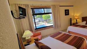 Quarto de hotel com duas camas, televisão, abajur e janela vista para piscina e árvores.