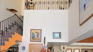 Um hall de hotel com balcão de recepção em madeira, piso de azulejos, escada e lustre.