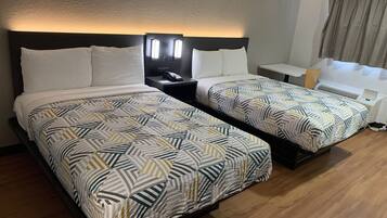 Quarto de hotel com duas camas, cada uma com roupa de cama estampada e cabeceira com iluminação embutida.