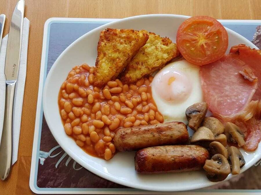 Um prato de comida de café da manhã com feijão, salsichas, ovos, bacon e uma fatia de tomate.