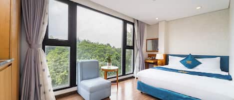 Quarto de hotel com uma grande janela, uma cama, uma mesinha e uma cadeira.