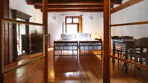 Quarto com piso de madeira, cama com estrutura de metal, mesa de madeira e uma cadeira.