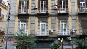 Um edifício com vários andares, varandas, aparelhos de ar condicionado e lojas na rua.