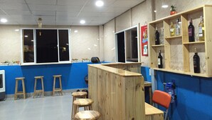 Interior de restaurante com parede azul de destaque, balcão de bar em madeira, banquetas e prateleiras com garrafas.