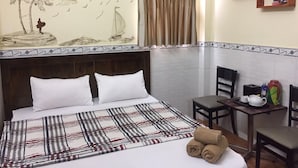 Quarto de hotel com cama, uma pequena mesa com cadeira, prateleira na parede e janela com cortinas.