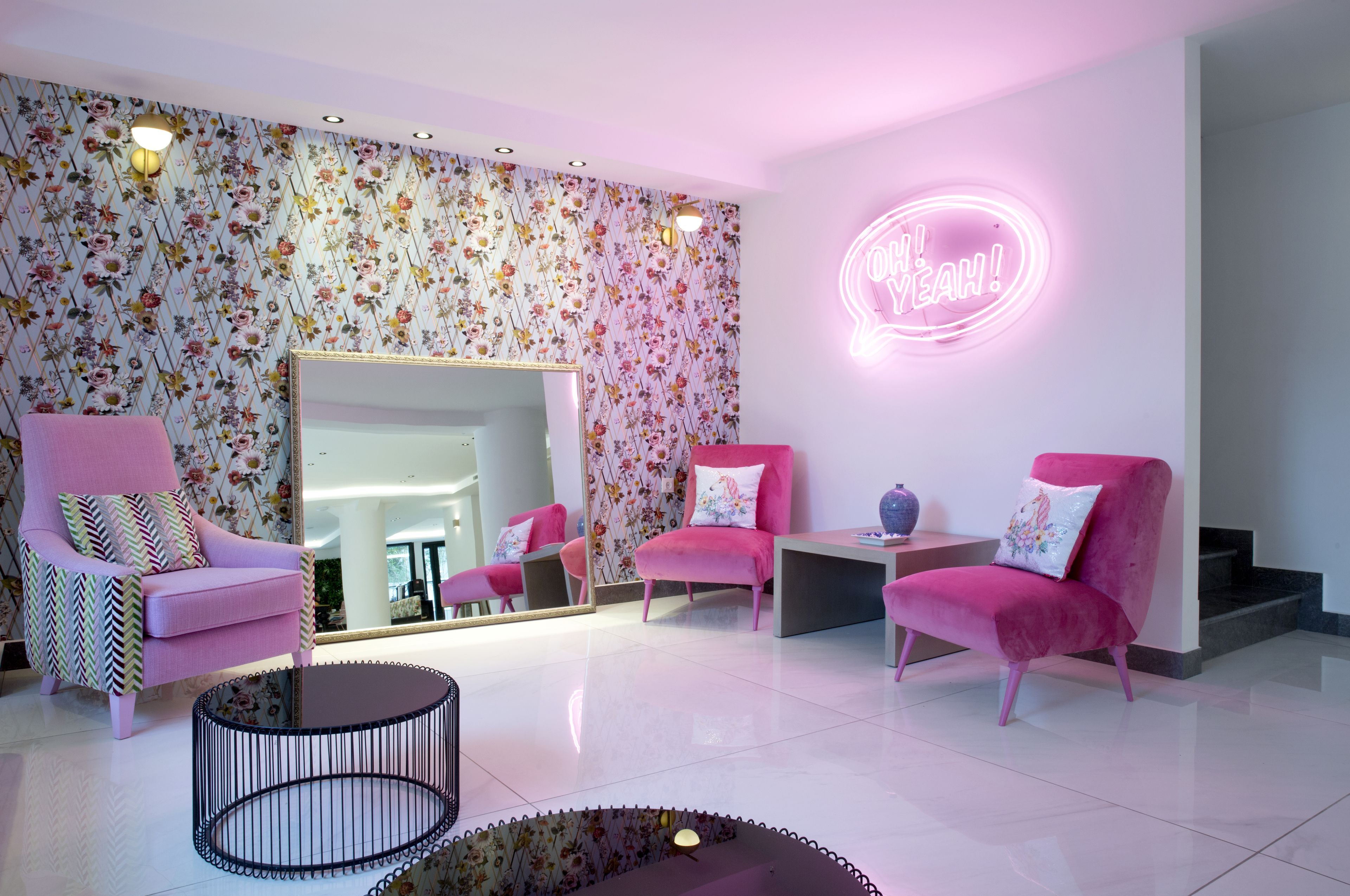 Quarto moderno com cadeiras cor-de-rosa, um espelho grande e um letreiro de neon 'Welcome!'.
