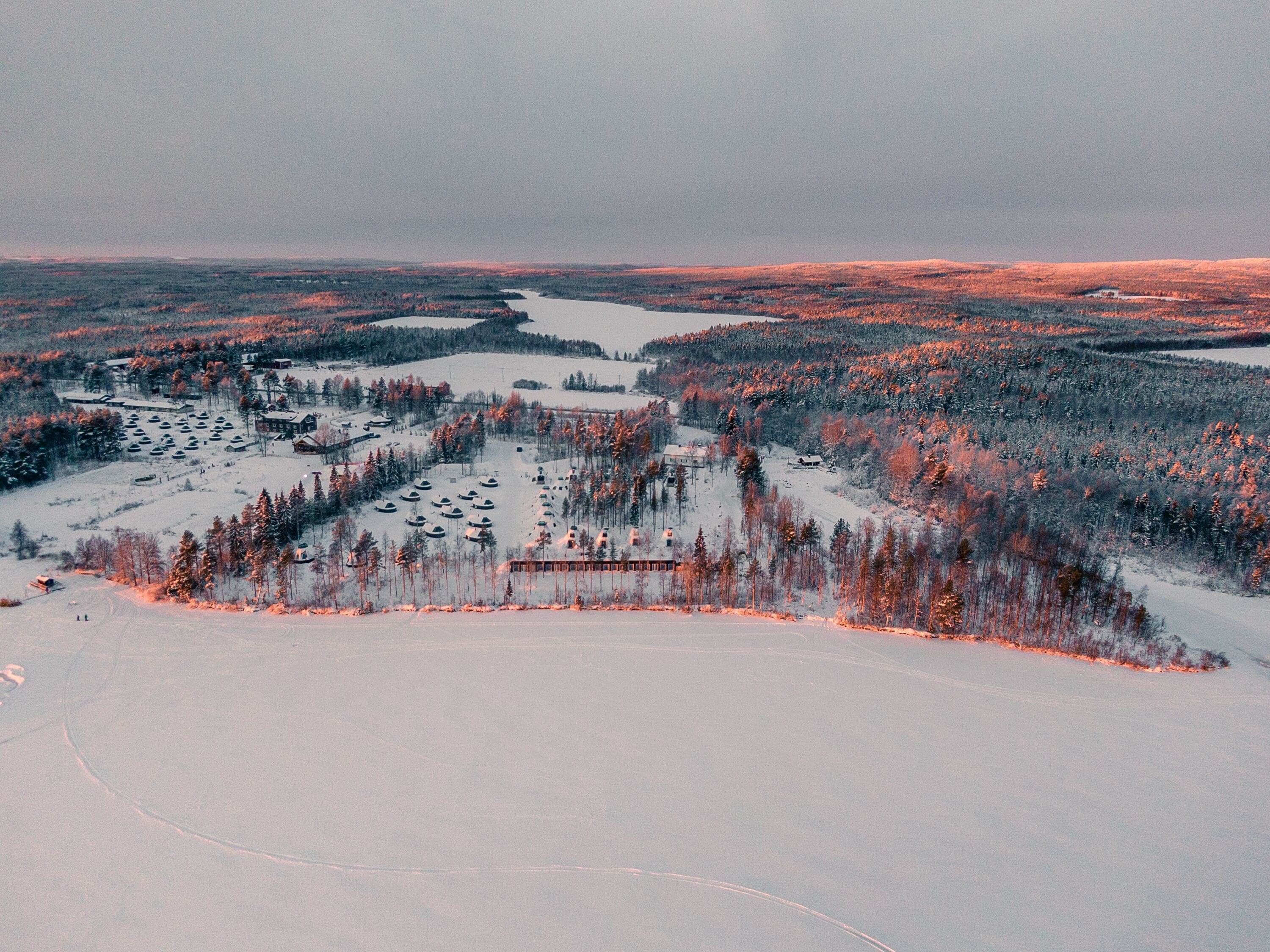 Vista aérea de uma paisagem coberta de neve, com cabanas e um lago.