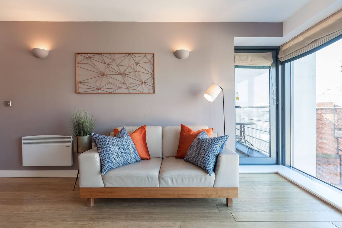 Uma sala de estar moderna com sofá, obras de arte decorativas, luminárias fixadas na parede e vista através de uma grande janela.