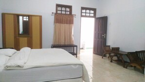 Quarto de hotel com cama, escrivaninha, duas cadeiras, janela com cortinas e porta.