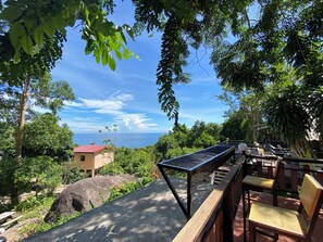 Um terraço com mesa e cadeiras, com vista para o mar e vegetação exuberante.