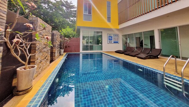 Piscina com deck revestido, um edifício amarelo com janelas amplas e uma placa indicando área de piscina.