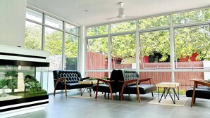 Um quarto espaçoso com grandes janelas, um aquário de vidro e uma área de estar moderna com poltronas de couro e uma mesa de madeira.