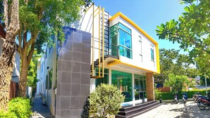 Um edifício moderno de dois andares com fachada de vidro, uma parede de destaque amarela e um caminho de acesso pavimentado.