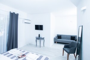 Quarto de hotel moderno com uma cama, um sofá cinzento, uma mesinha e uma televisão fixada na parede.