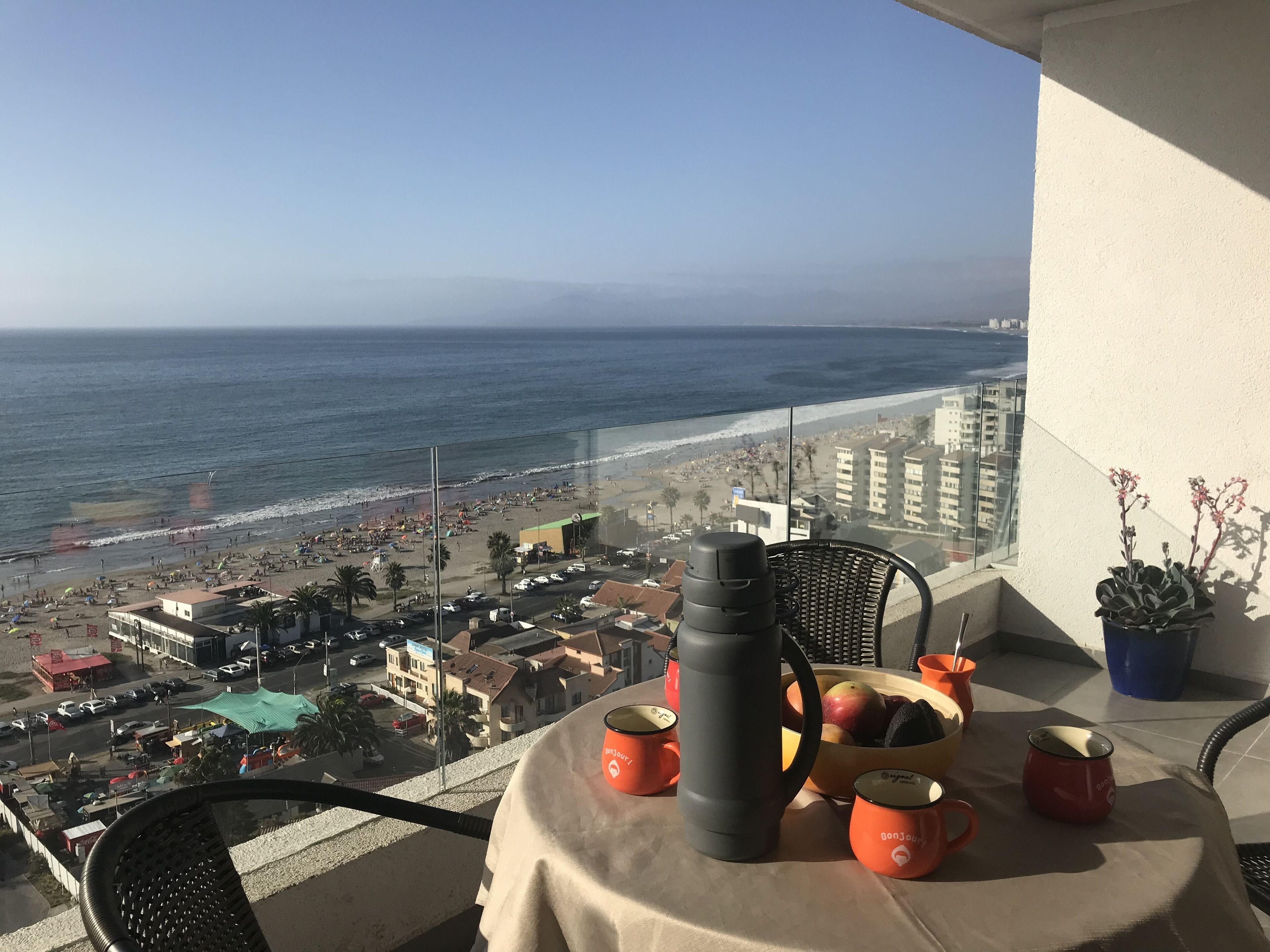 Varanda com mesa posta para dois, com vista para a praia e o horizonte urbano.