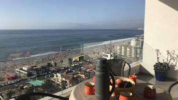 Varanda com mesa posta para dois, com vista para a praia e o horizonte urbano.