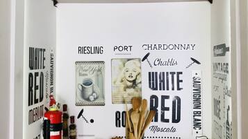 Uma bancada de cozinha com vários frascos, um extintor de incêndio vermelho, utensílios de madeira e uma lousa com texto sobre vinho.