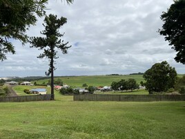 Paisagem rural com casas, um quintal cercado e céu nublado.