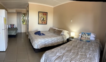 Quarto de hotel com duas camas, uma mesinha com luminária, um refrigerador e um quadro na parede.