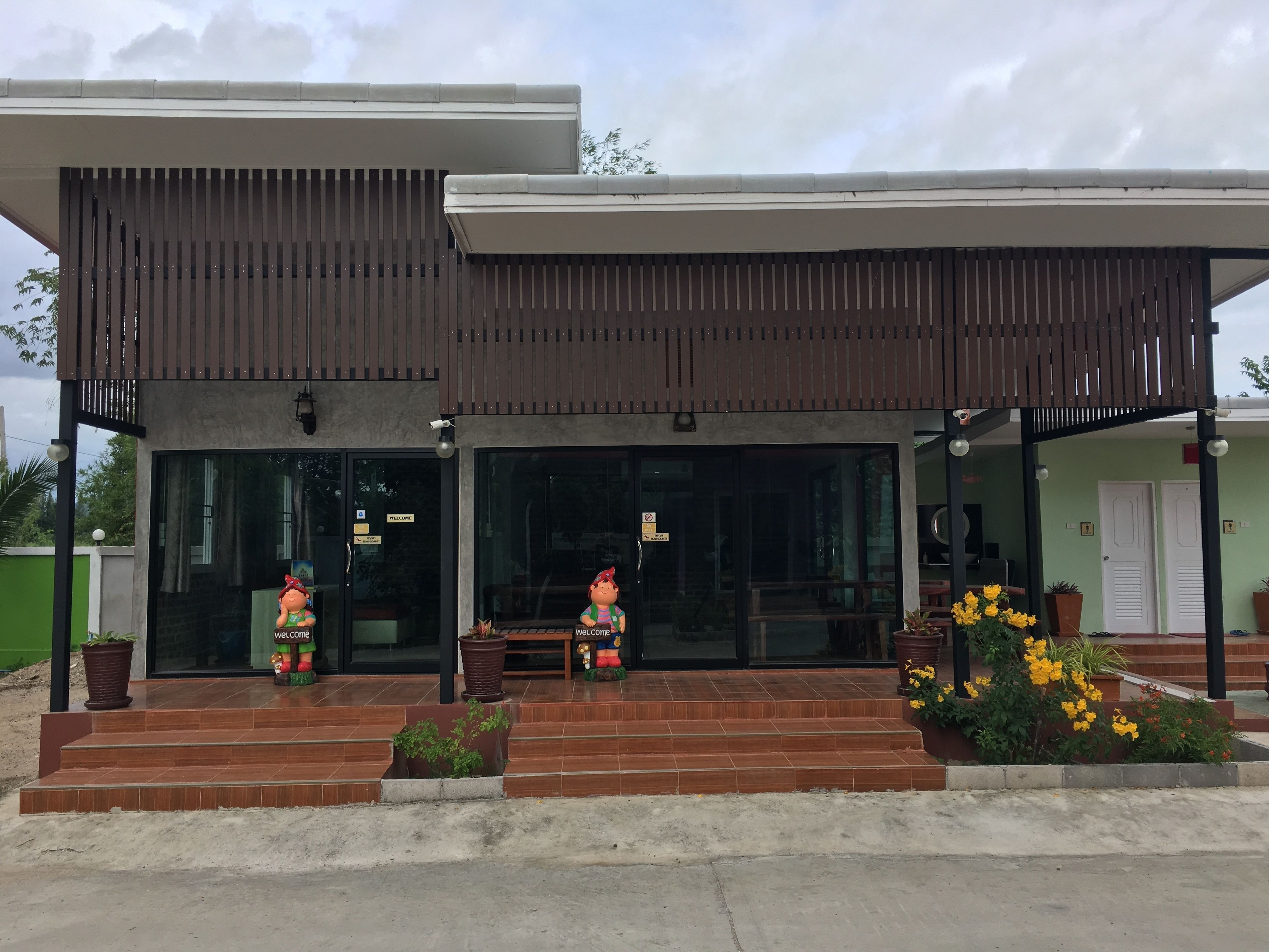 Um edifício moderno com estrutura em dois andares, grandes janelas de vidro e uma entrada convidativa com degraus e plantas em vasos.