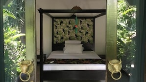 Uma cama de dossel com cabeceira estampada com pássaros, uma luminária pendente pequena e uma porta com puxador em formato de touro.