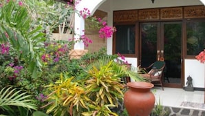 Um edifício branco com varanda de madeira, uma janela grande e um vaso com planta em primeiro plano.